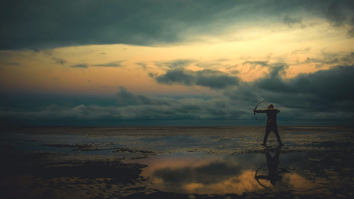 Man with a an arch and arrow in a beach